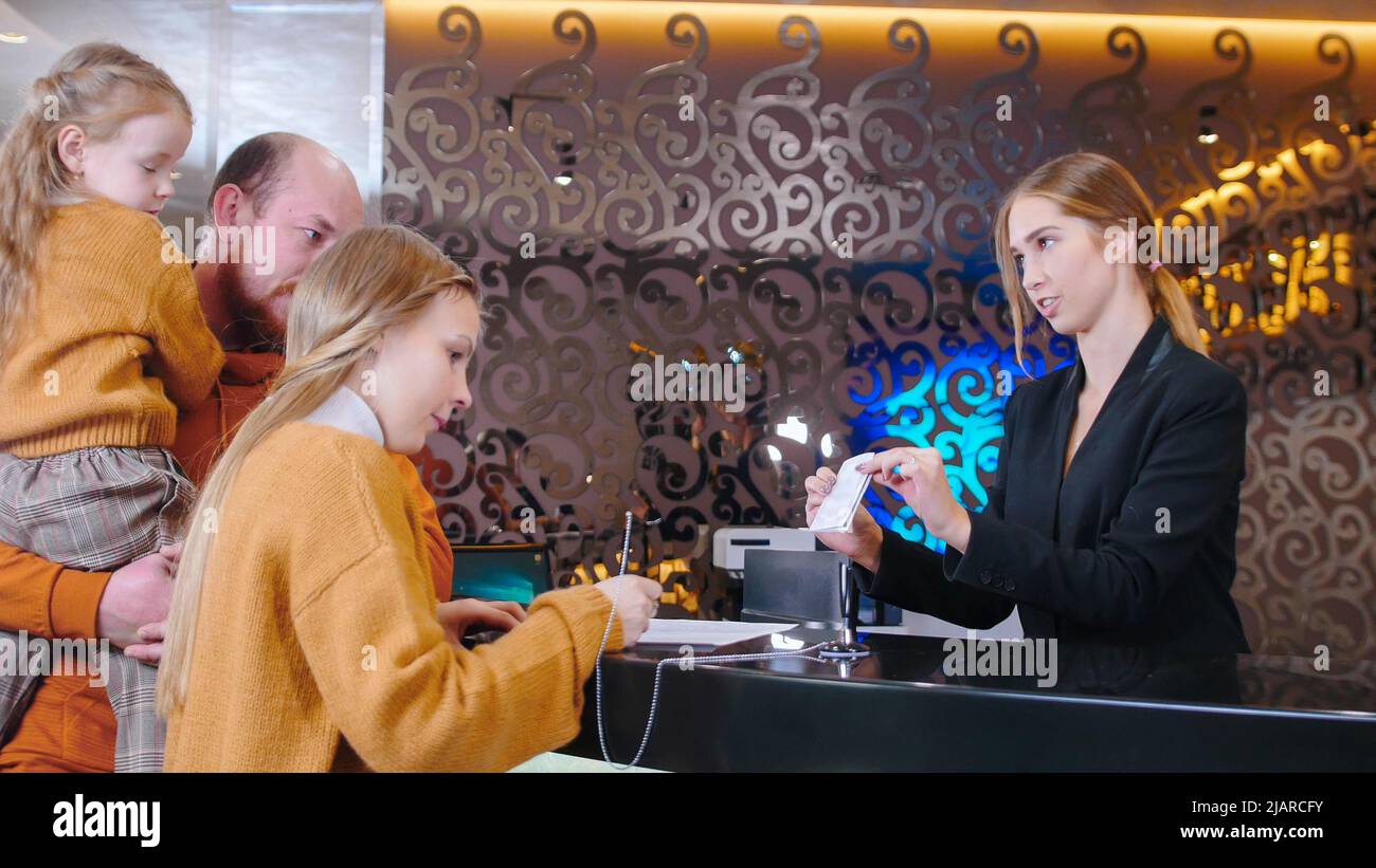 A family checking in the hotel - a woman on the reception greeting the ...