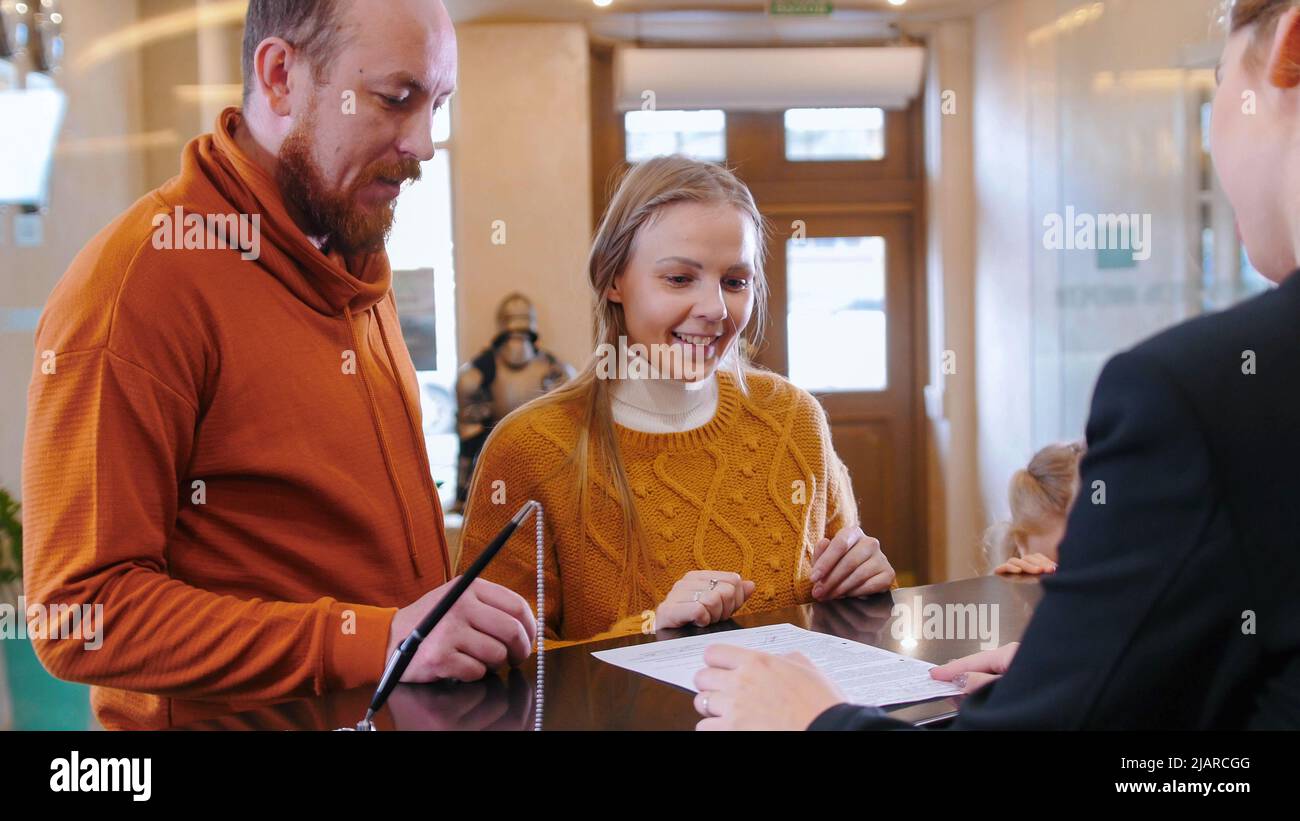 A family checking in the hotel - a woman looking at the papers for room ...