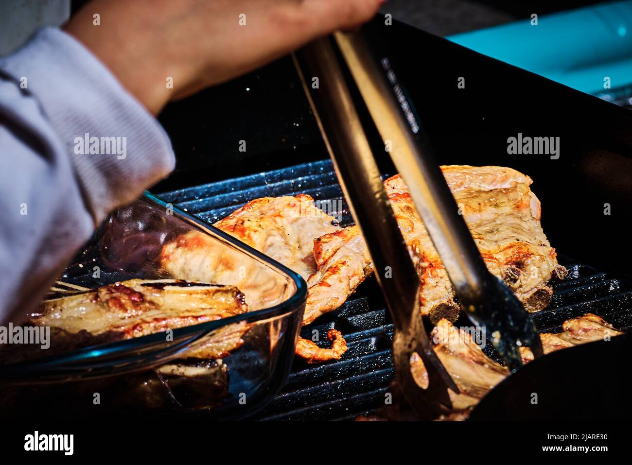 hand with a clamp placing the meat on a barbecue while cooking slowly ...