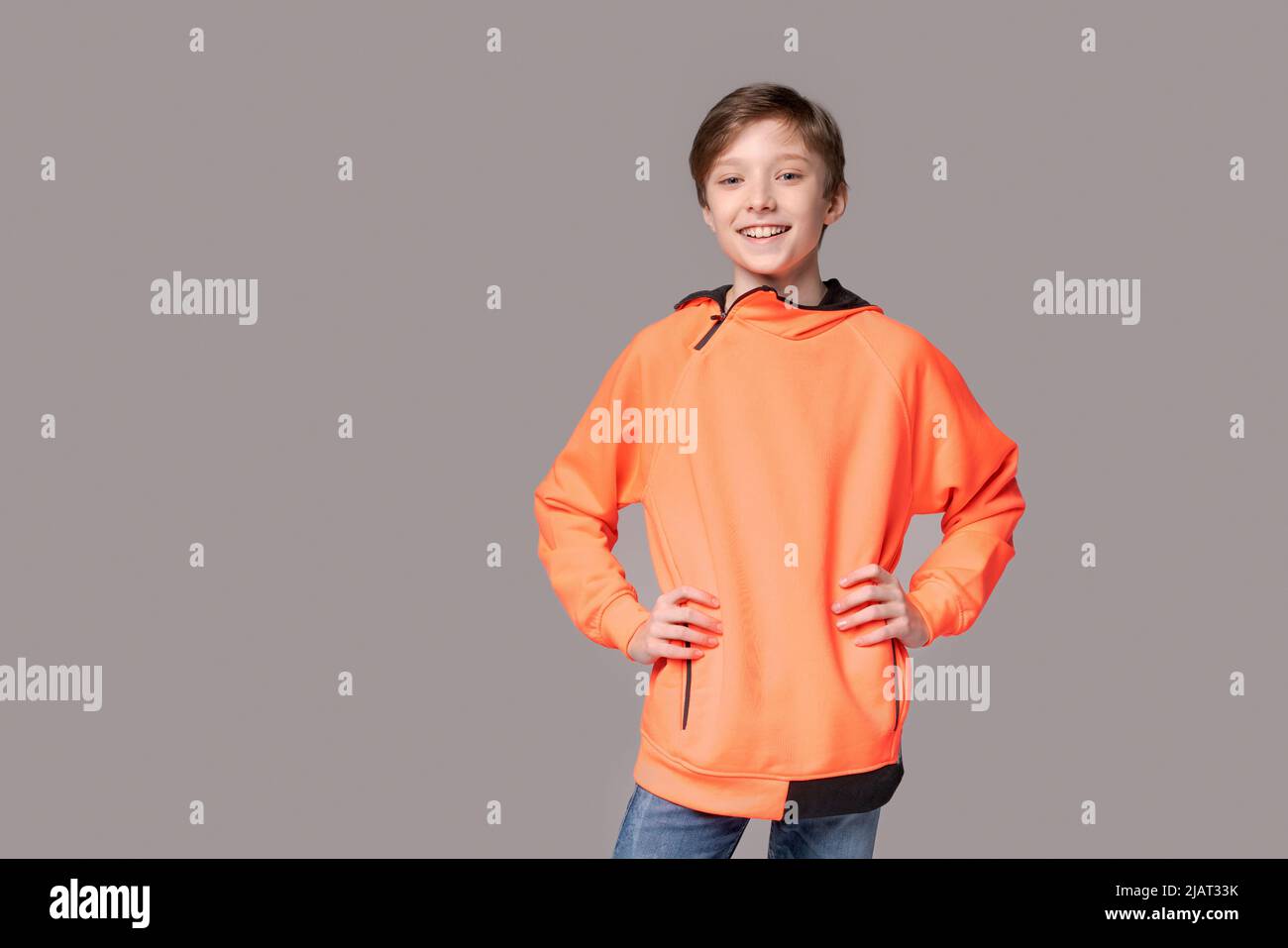 Portrait happy caucasian teenager man in orange sweatshirt on gray ...