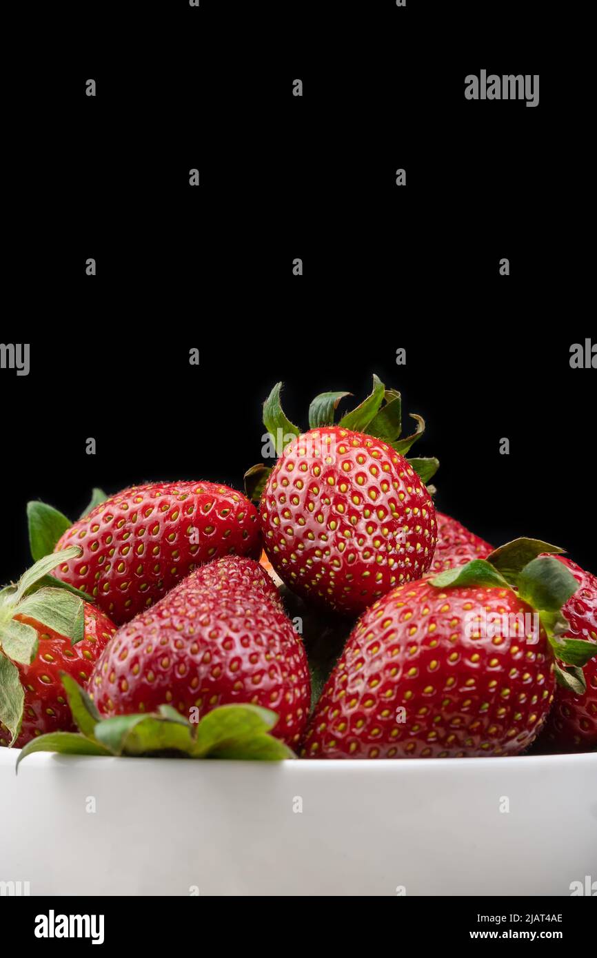 Close up ripe red strawberries with green tails in a white plate on a ...