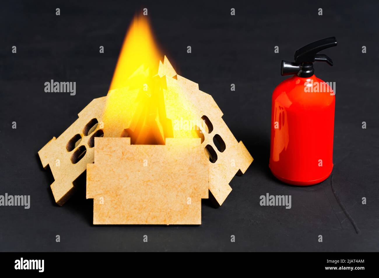 Miniature red fire extinguisher placed by a collapsed burning toy house ...
