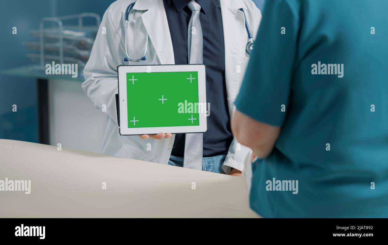 Male doctor holding horizontal green screen on digital tablet at ...