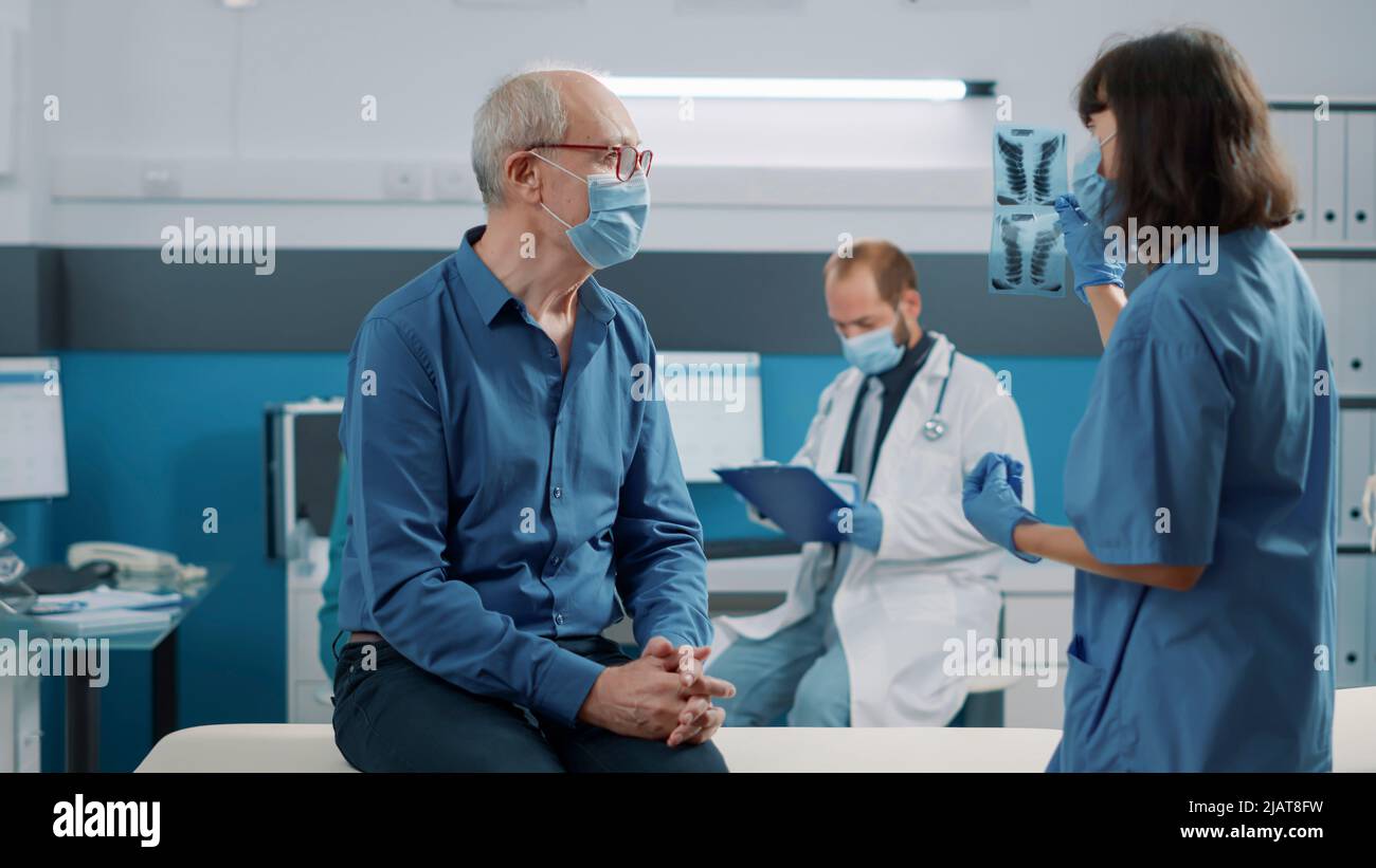 Female nurse explaining radiography scan diagnosis in cabinet to elder ...