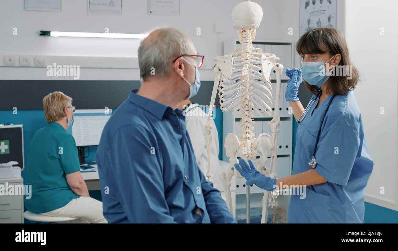 Nurse with face mask explaining bones on human skeleton, talking about ...