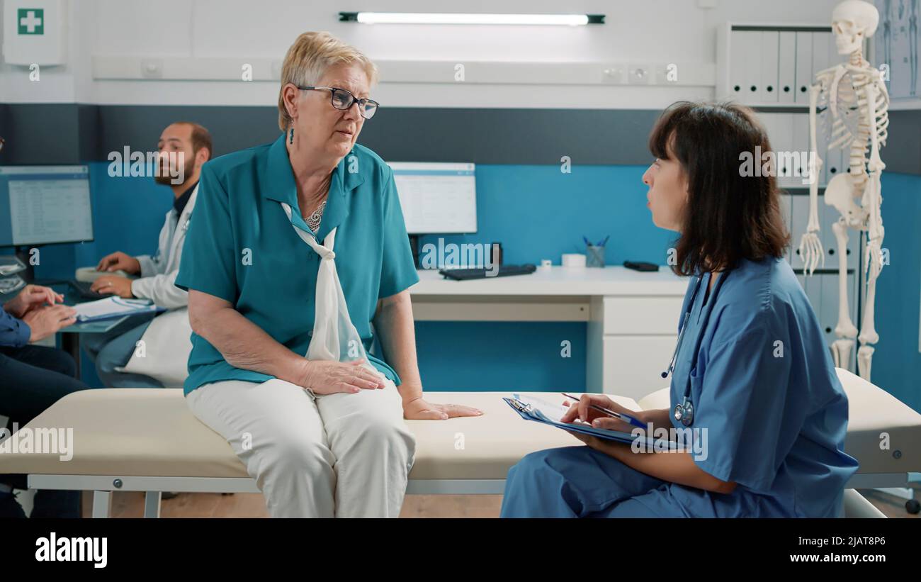 Senior woman having conversation with medical assistant at checkup ...
