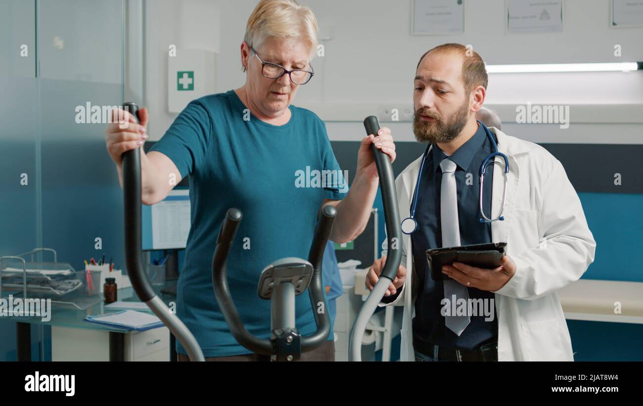 Male doctor examining senior woman on stationary bicycle, helping with ...
