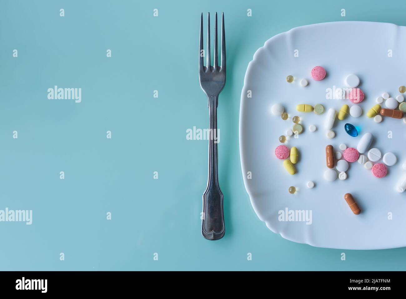 A handful of pills, capsules and multi-colored tablets on a plate next ...
