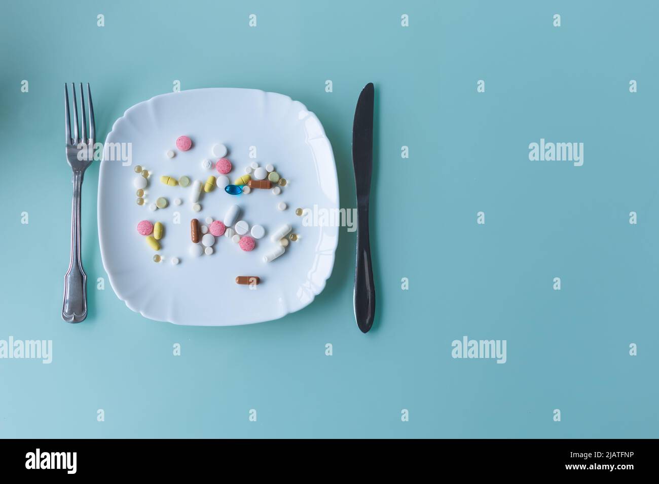 A handful of pills, capsules and multi-colored tablets on a plate next ...