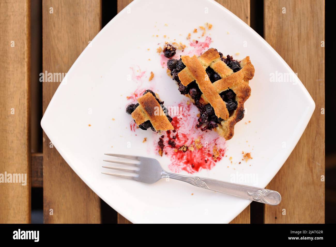 Remains of homemade lattice blueberry pie in square white plate with ...