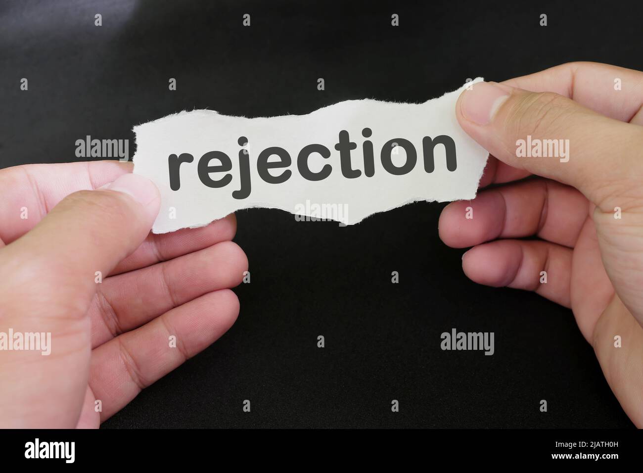 Hand holding a paper with written word rejection in black background ...