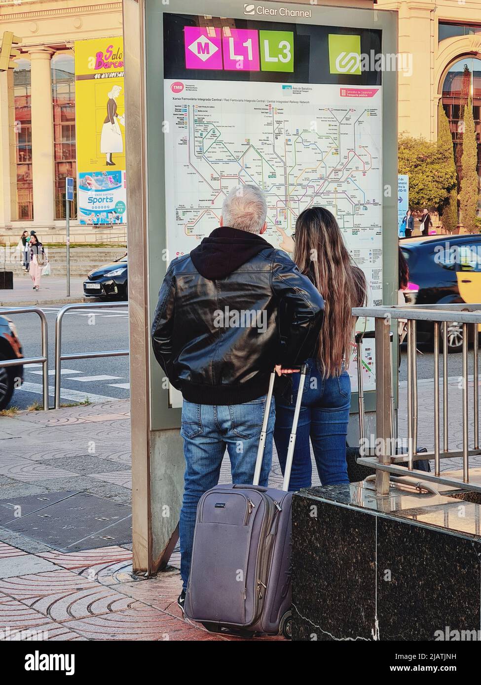 A couple of travelers in front of the Barcelona subway map pointing to ...