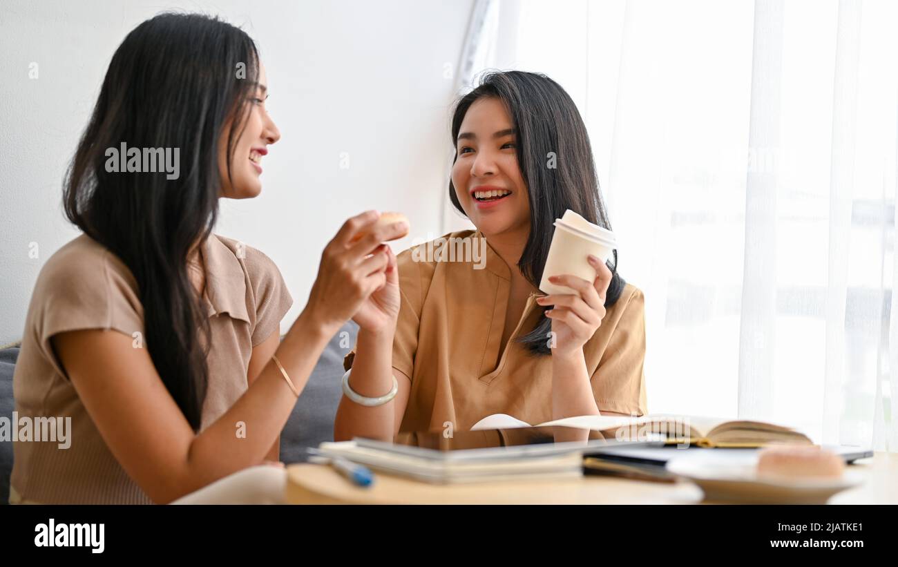 Cheerful and beautiful Asian women enjoy chatting, eating a yummy snack ...