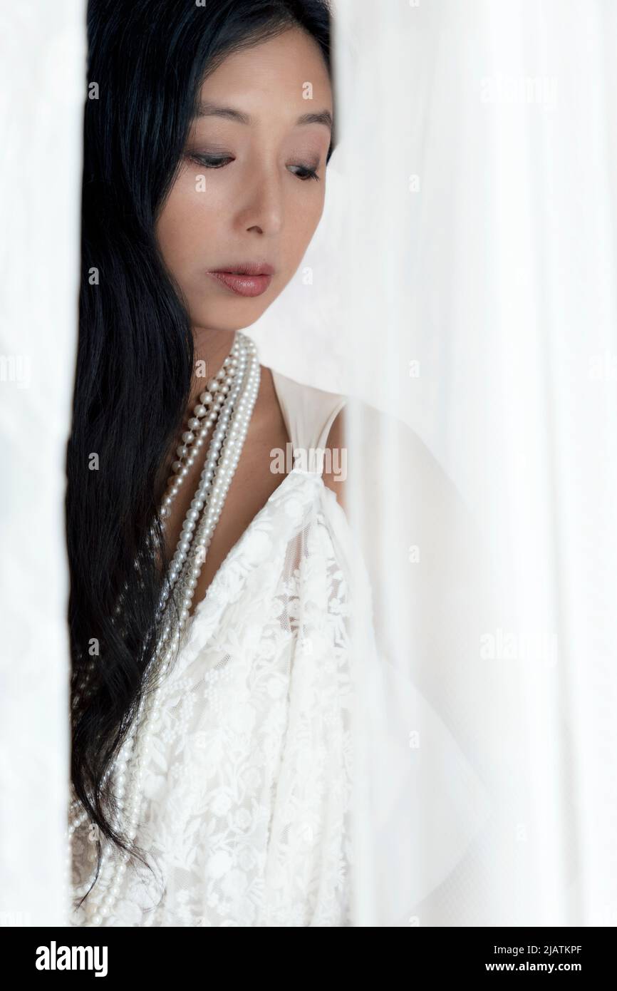 A beautiful Asian woman wearing a white lace dress and posing amongst ...
