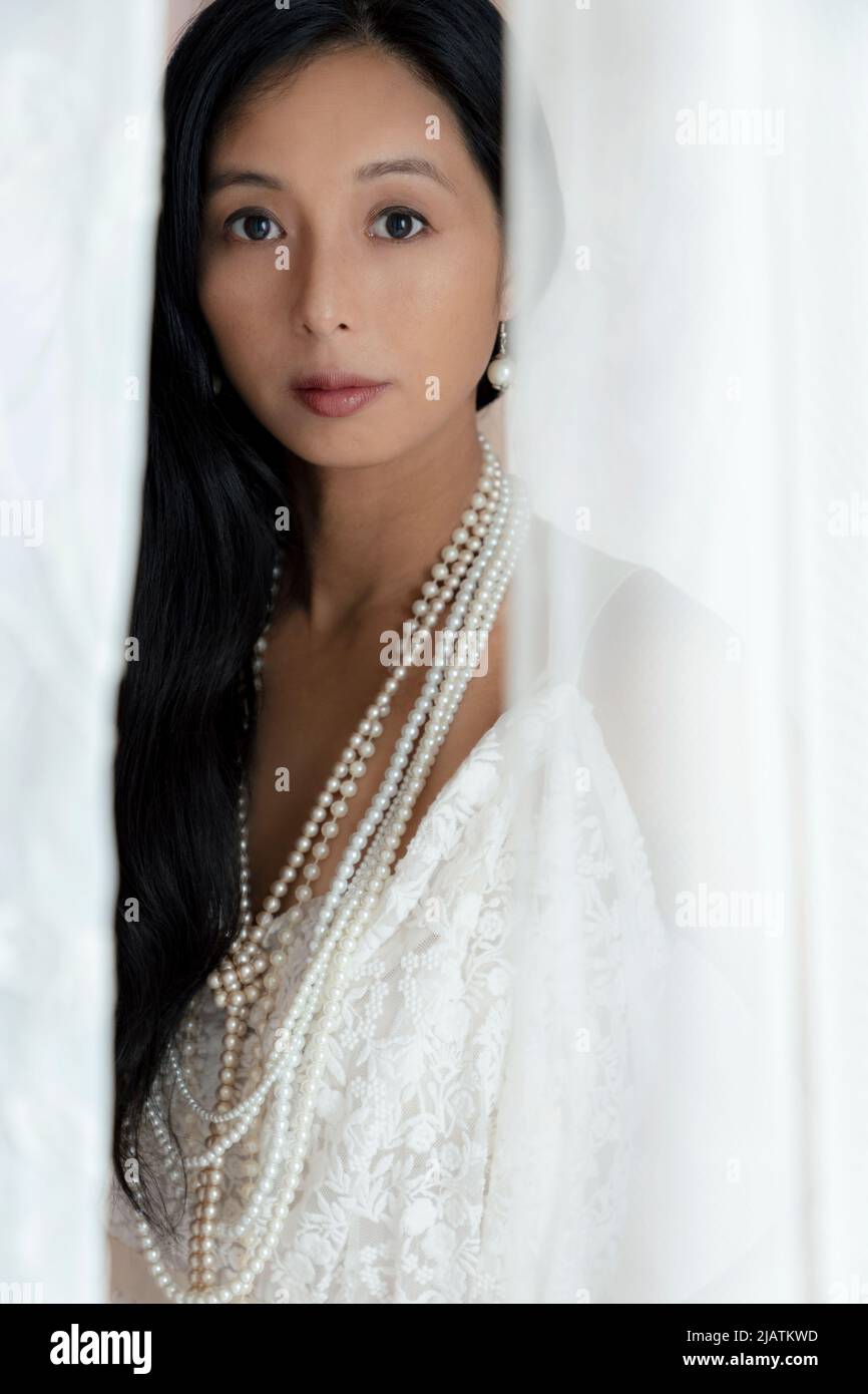 A beautiful Asian woman wearing a white lace dress and posing amongst ...