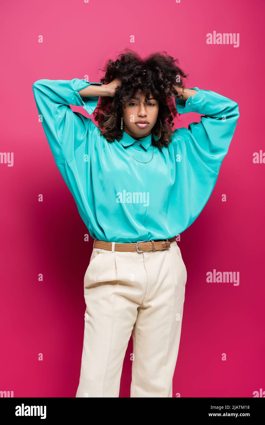 trendy african american woman in turquoise blouse touching curly hair ...