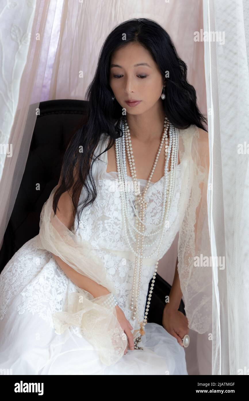 A beautiful Asian woman wearing a white lace dress and posing amongst ...