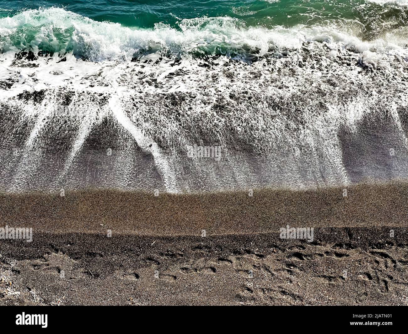 A gentle surf washes on Black Beach disclosing the different colors of ...