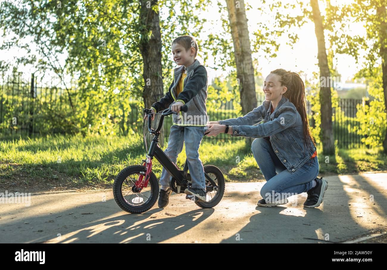 Mom helps a child boy learn to ride a two-wheeled bicycle in the park ...