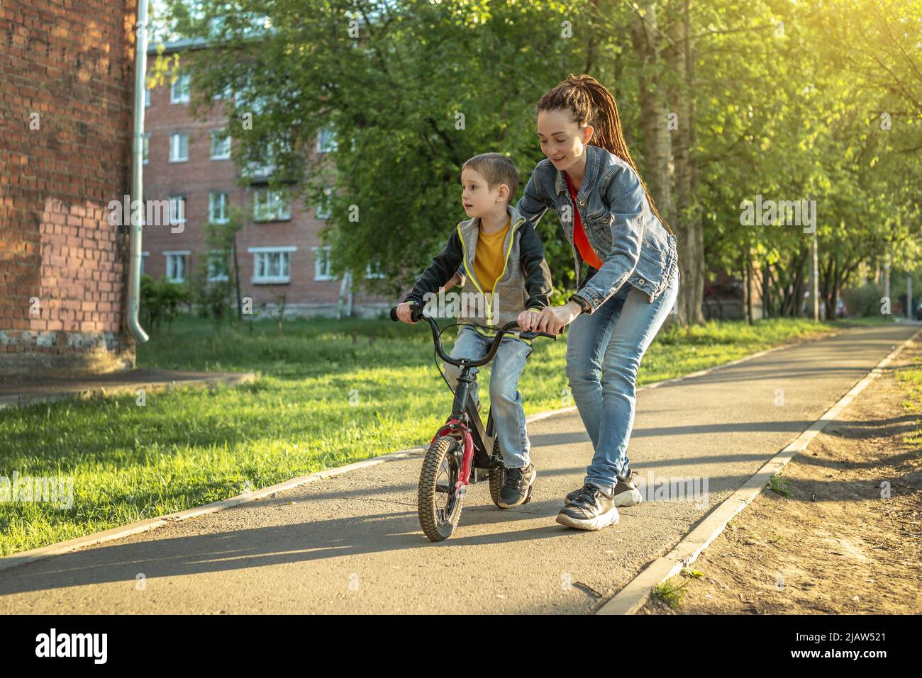 Mom helps a child boy learn to ride a two-wheeled bicycle in the park ...