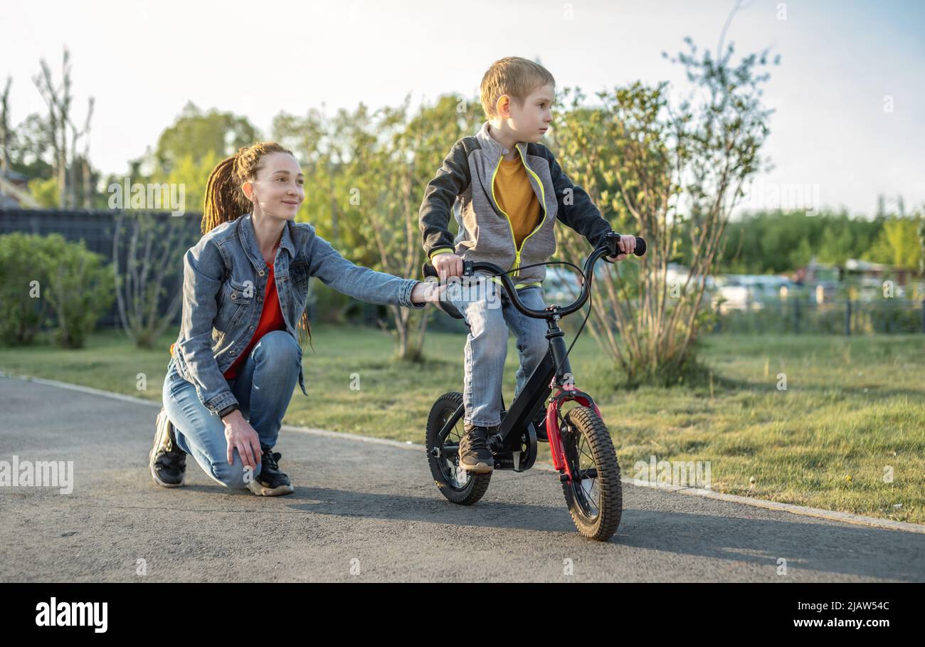 Mom helps a child boy learn to ride a two-wheeled bicycle in the park ...