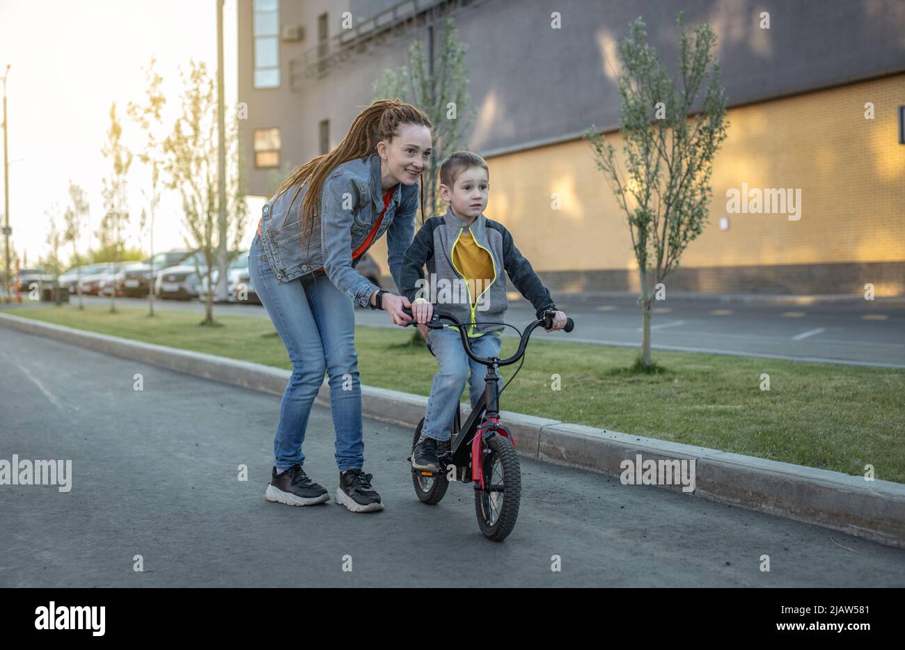 Mom helps a child boy learn to ride a two-wheeled bicycle in the park ...