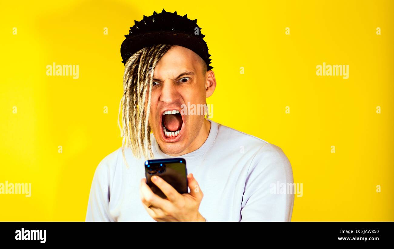 Young aggressive man shouts into mobile phone. Angry excited guy with ...