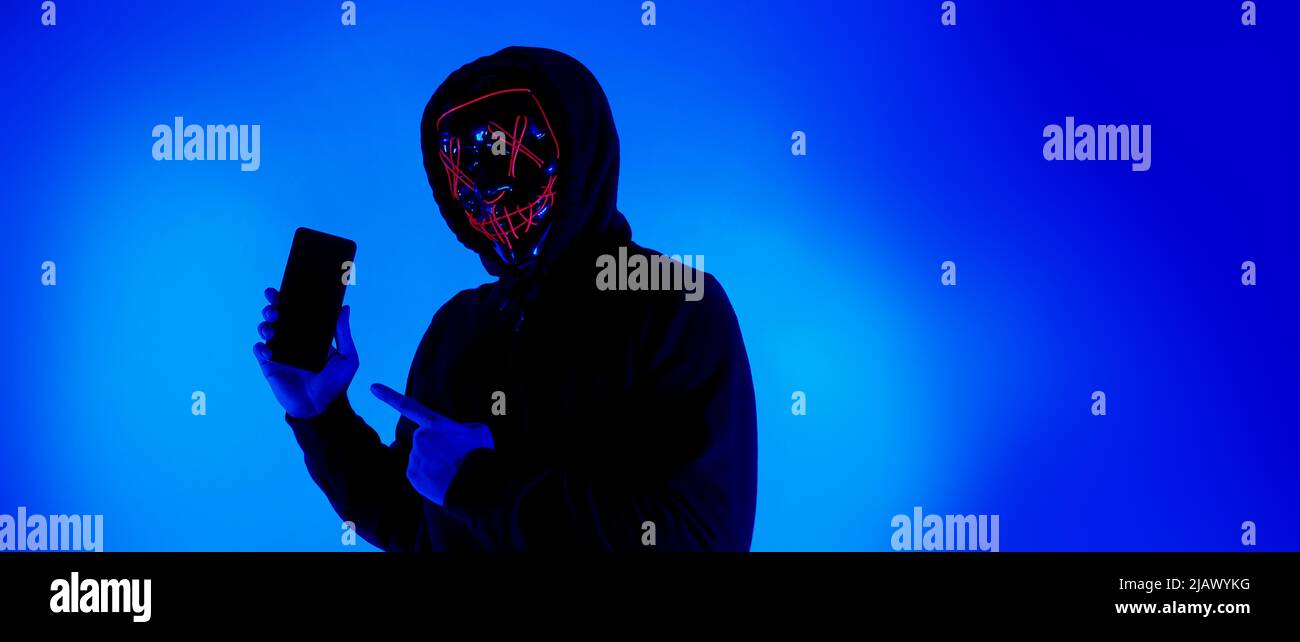 Anonymous hacker and face mask with smartphone in hand. Man in black ...