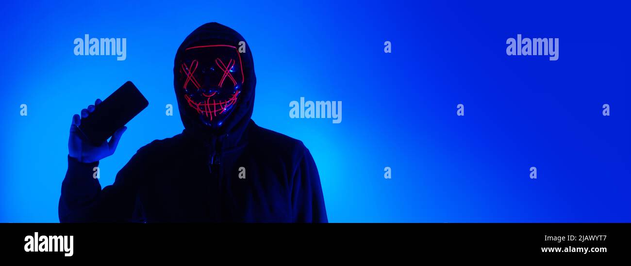 Anonymous hacker and face mask with smartphone in hand. Man in black ...