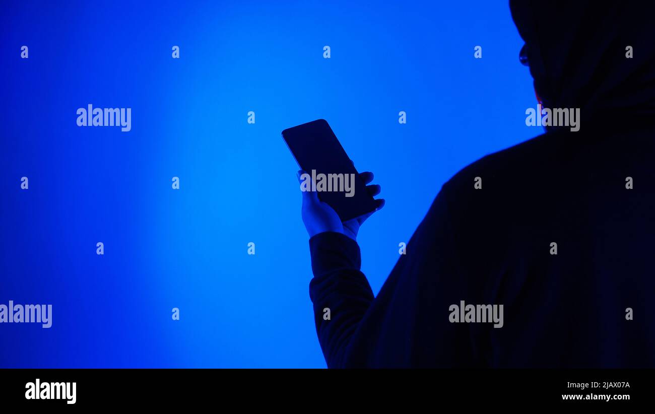 Anonymous hacker and face mask with smartphone in hand. Man in black ...