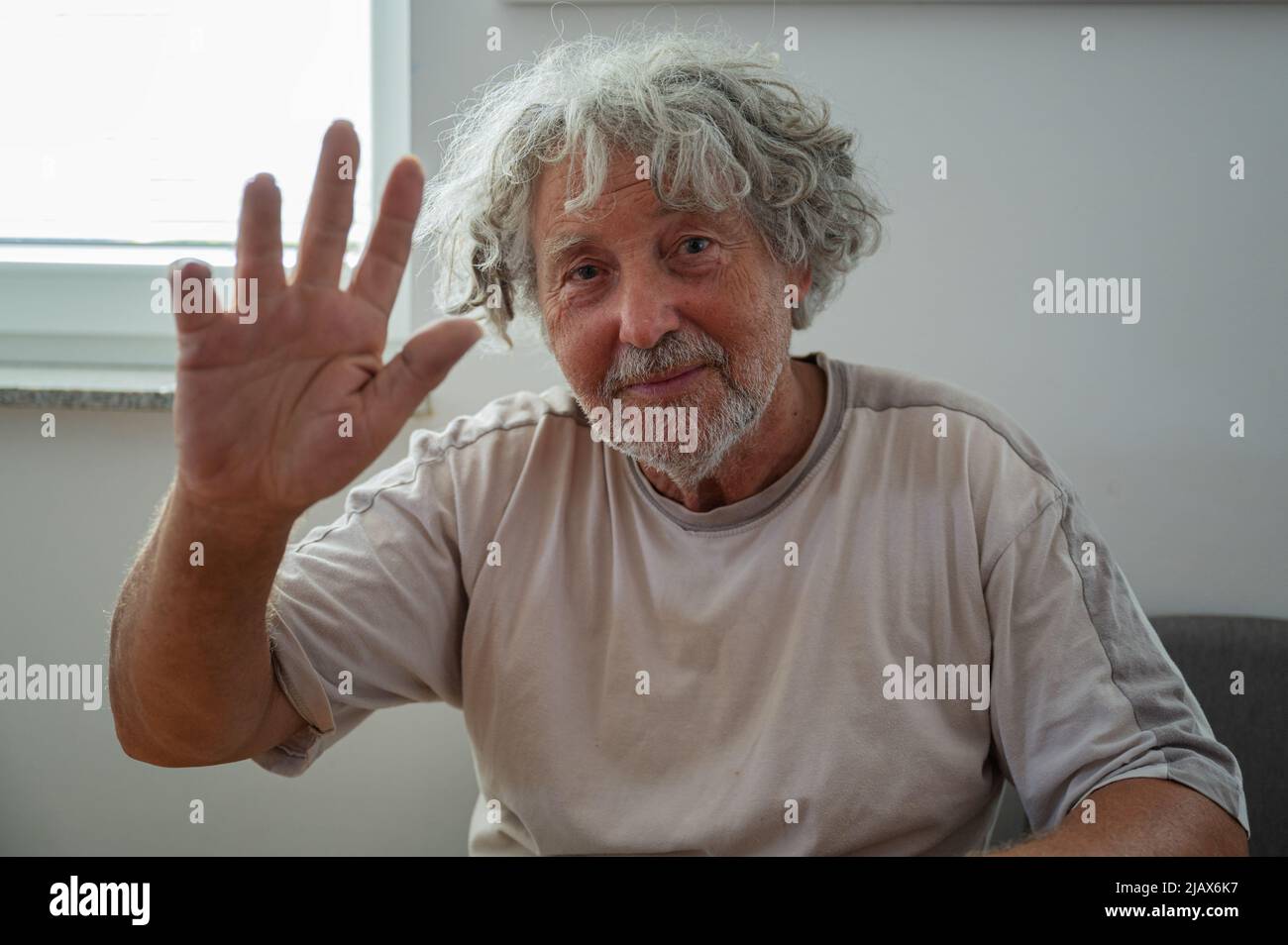 Authentic senior man, grandpa, with grey curly hair waving with his ...