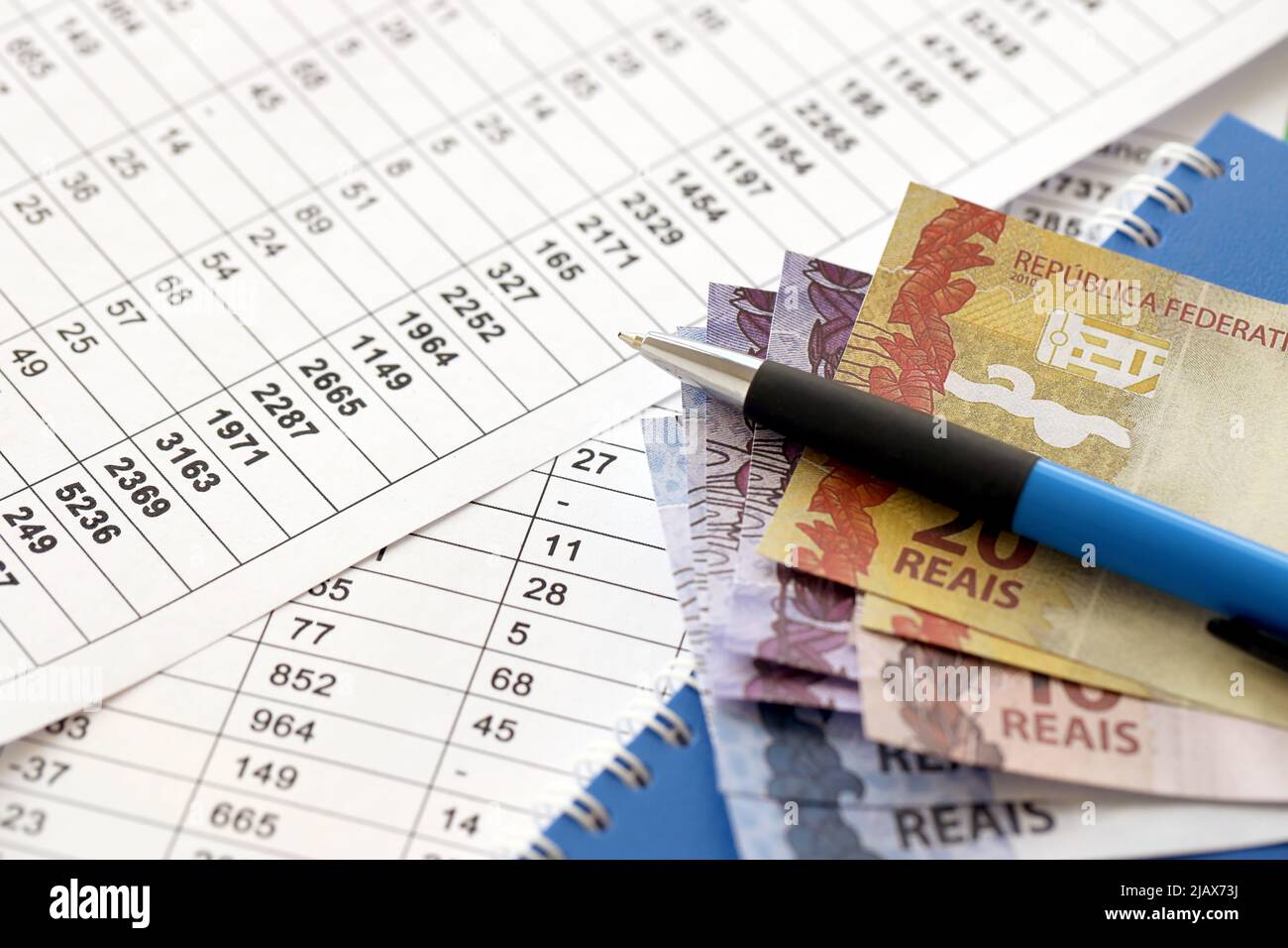 Pen with Brazilian money bills on documents with calculations table ...