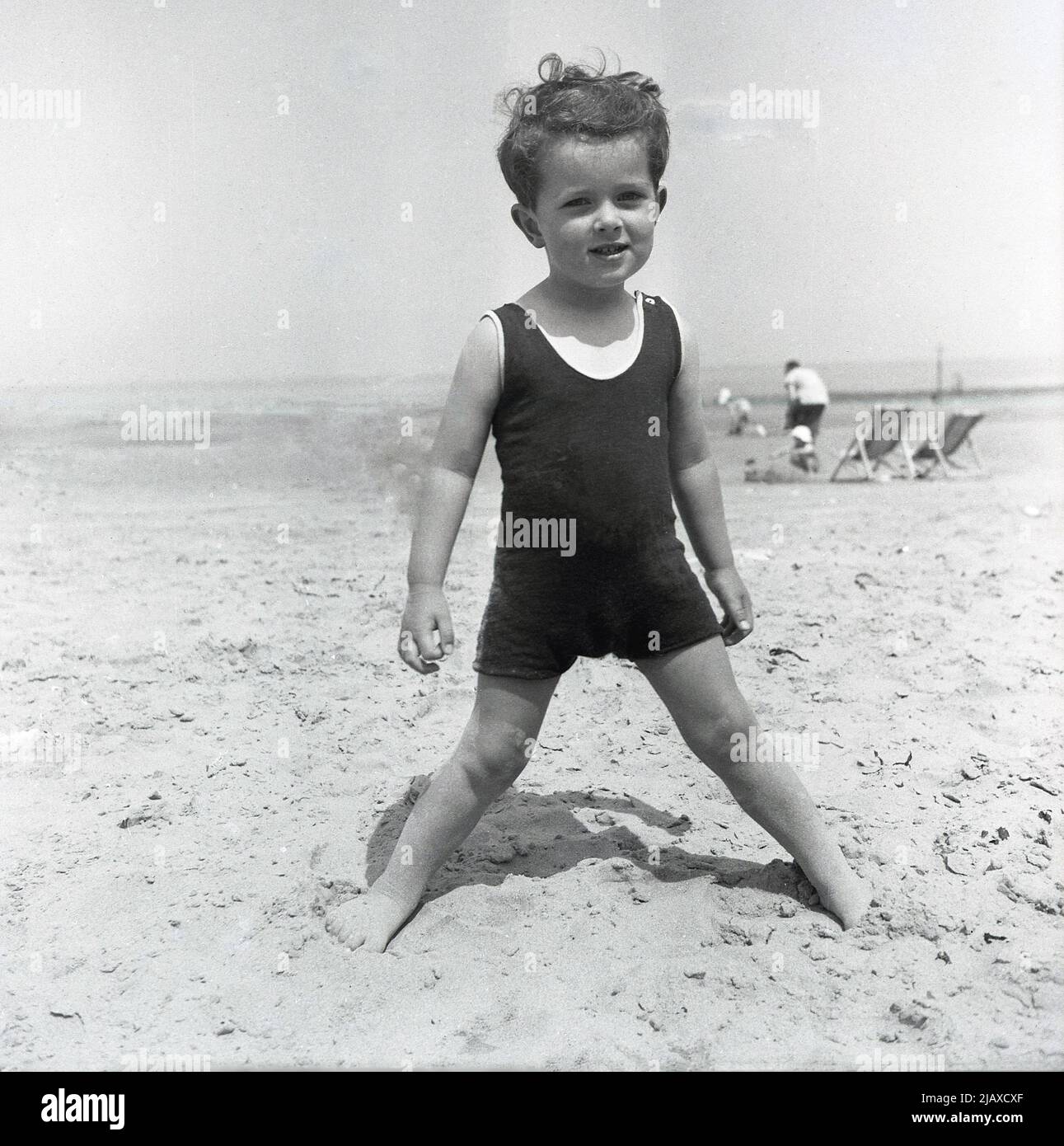 1950s, historical, a young boy standing on the sand on a beach in the ...