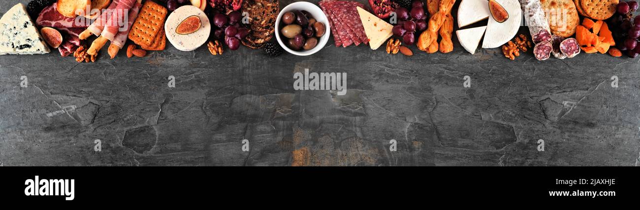 Assorted cheese and meat appetizers. Overhead view top border on a dark ...