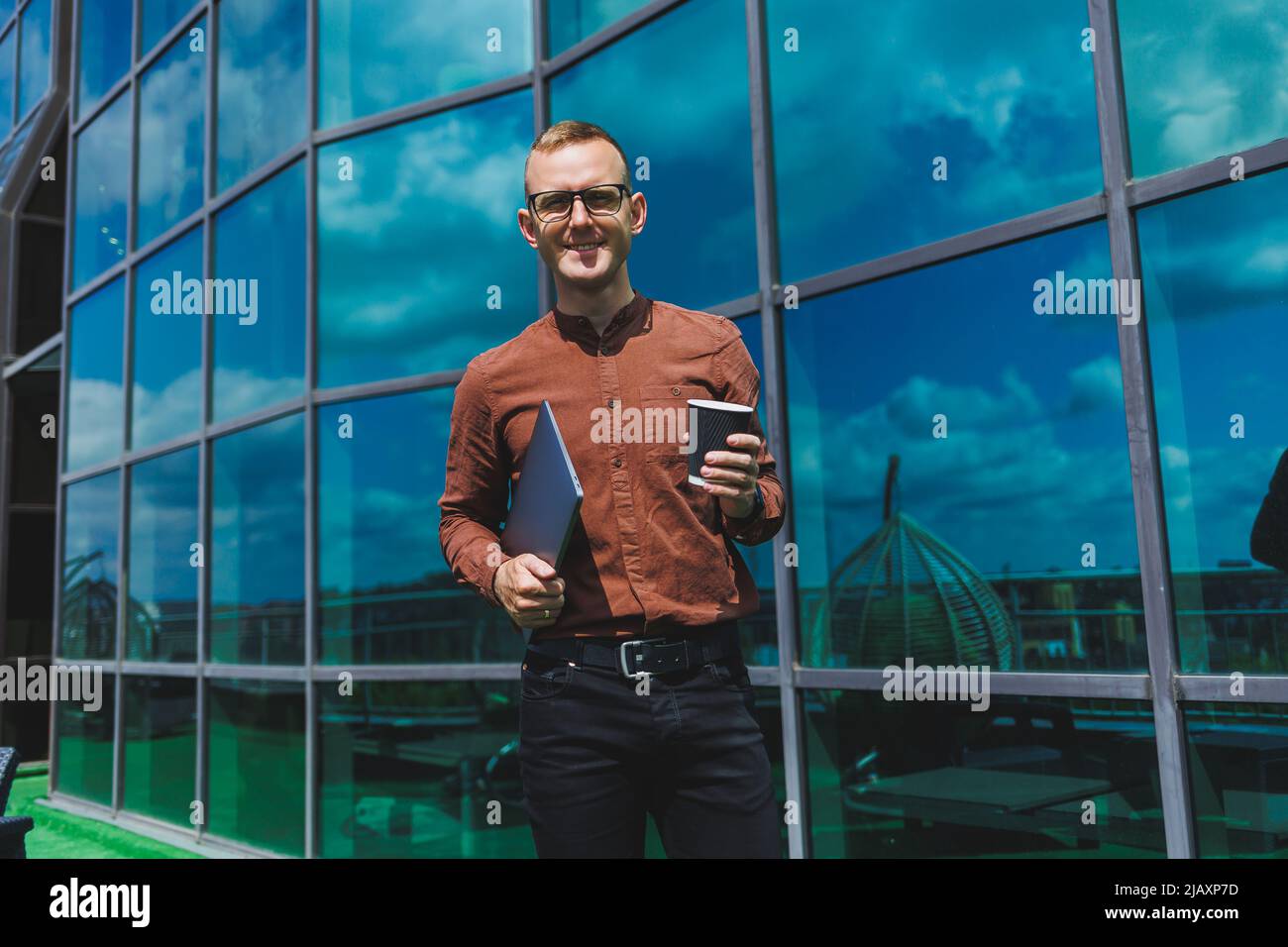 A young handsome attentive man in glasses with a laptop and a glass of ...
