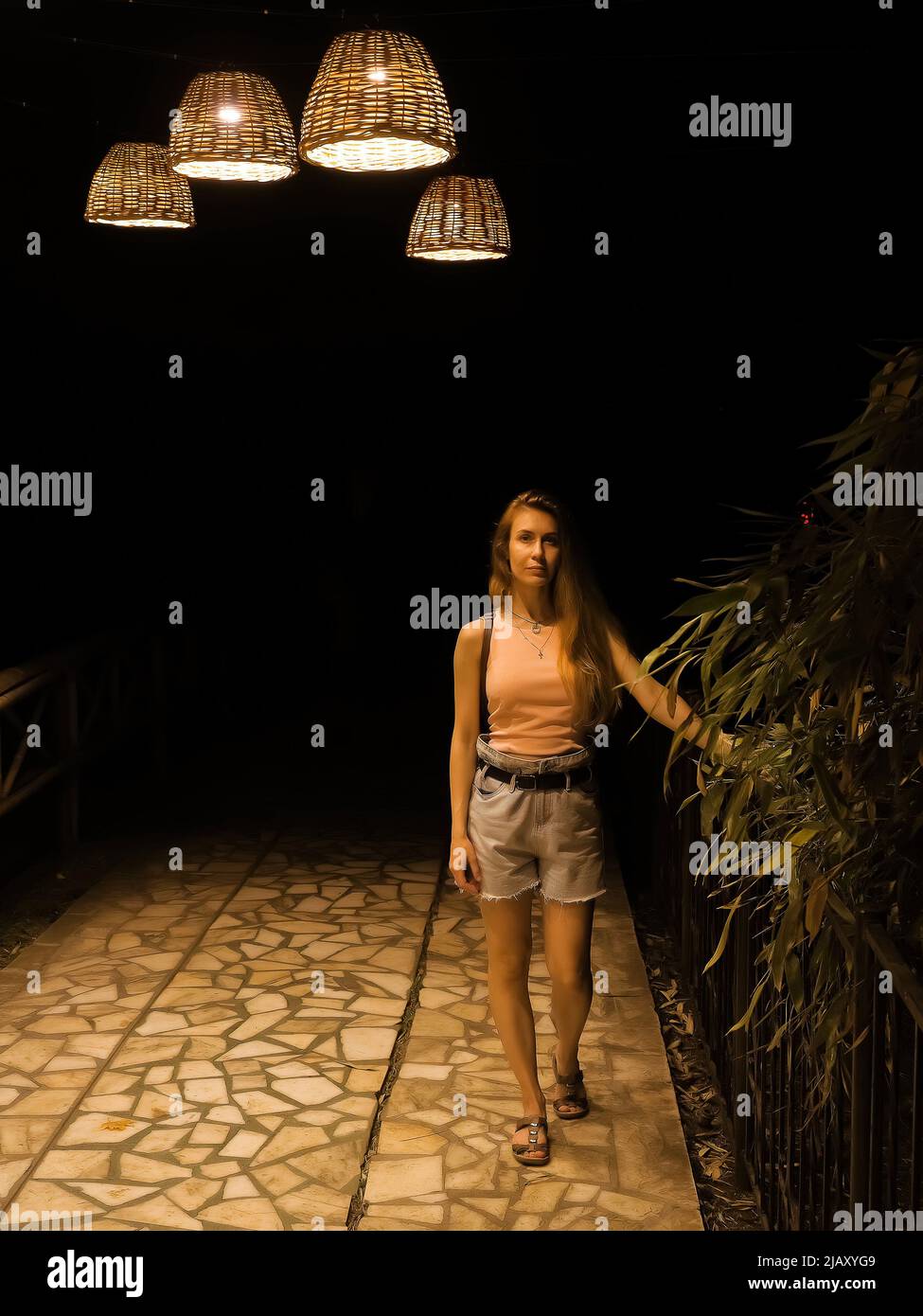 A woman stands on a marble path in a park bamboo alley at night ...