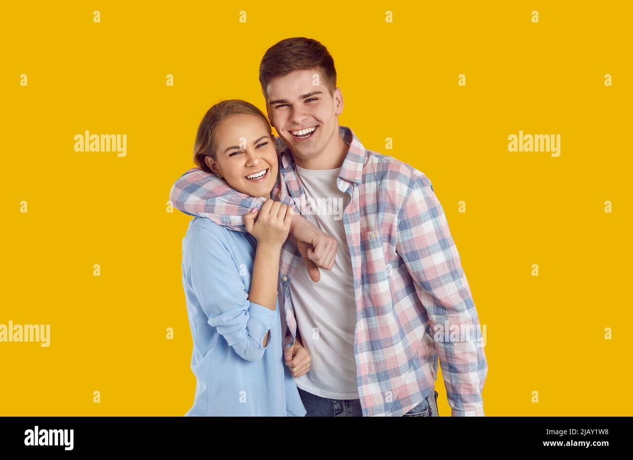 Studio portrait of cheerful siblings or teen couple hugging each other ...