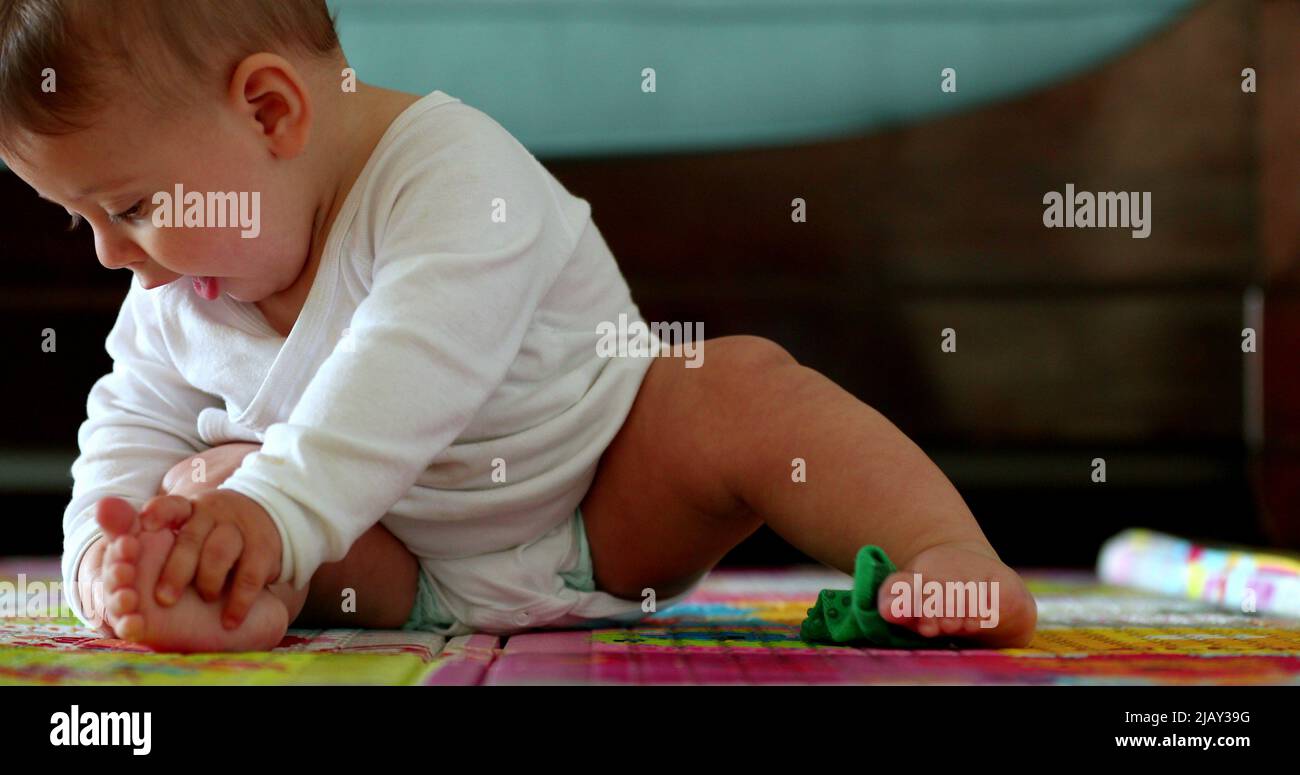 Cute baby toddler infant child on play mat wanting to bite his own feet ...