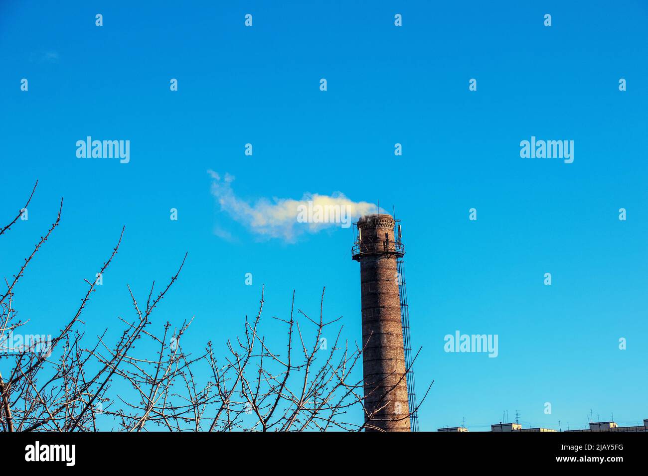 White-yellow smoke from the chimney of the boiler room against the blue ...