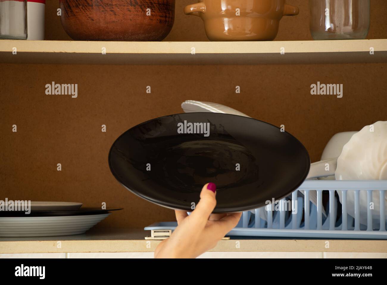 The girl takes out a plate from the shelf of the kitchen cabinet, a ...