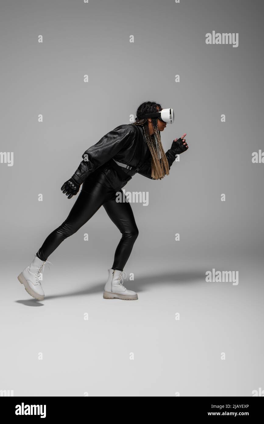 Side view of african american woman in vr headset running on grey ...