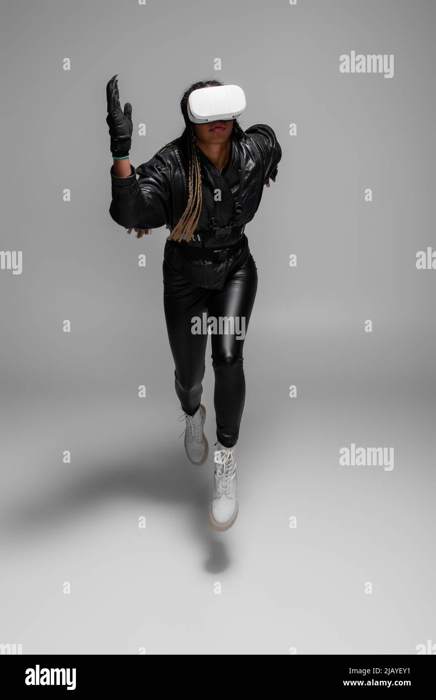 African american woman in leather gloves and vr headset running on grey ...