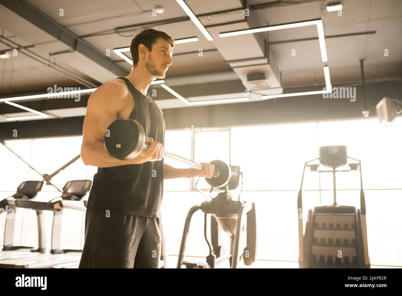Serious young man lifting barbells looking focused, working out in a ...