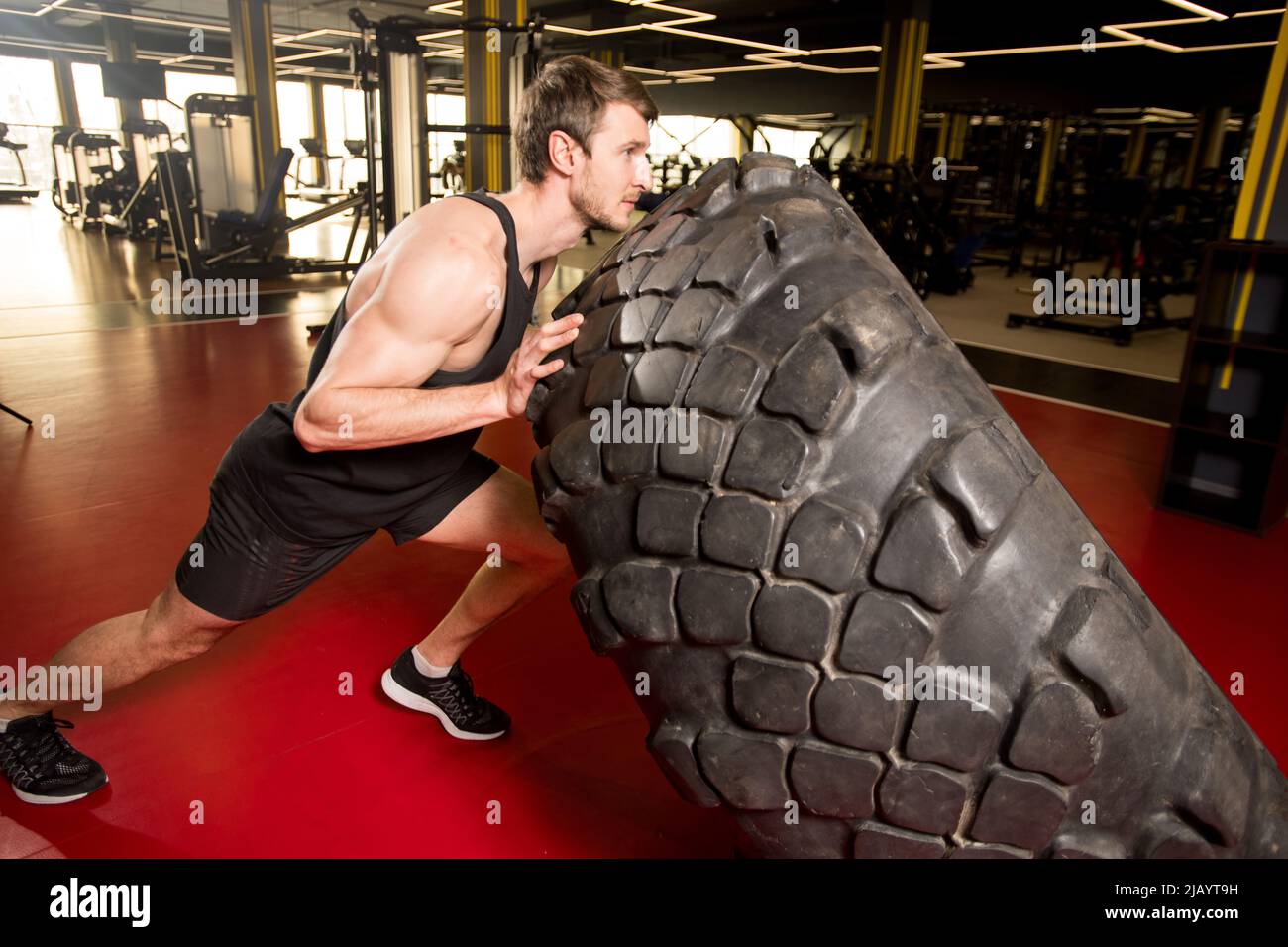 Strong muscular man working out with a huge tire, he raising and ...