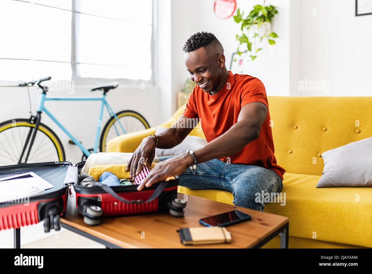 Young african man packing clothes to luggage before going on summer ...