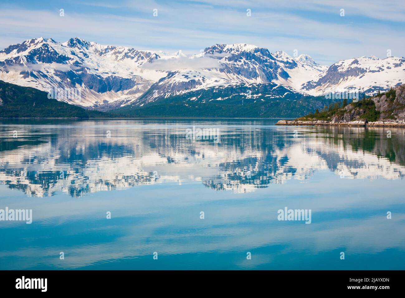 Snow covered mountains and blue sky reflected in the calm, smooth water ...