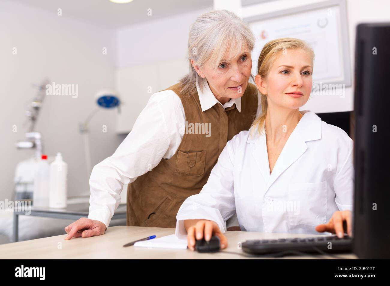 Young woman dermatologist using computer with patient during ...