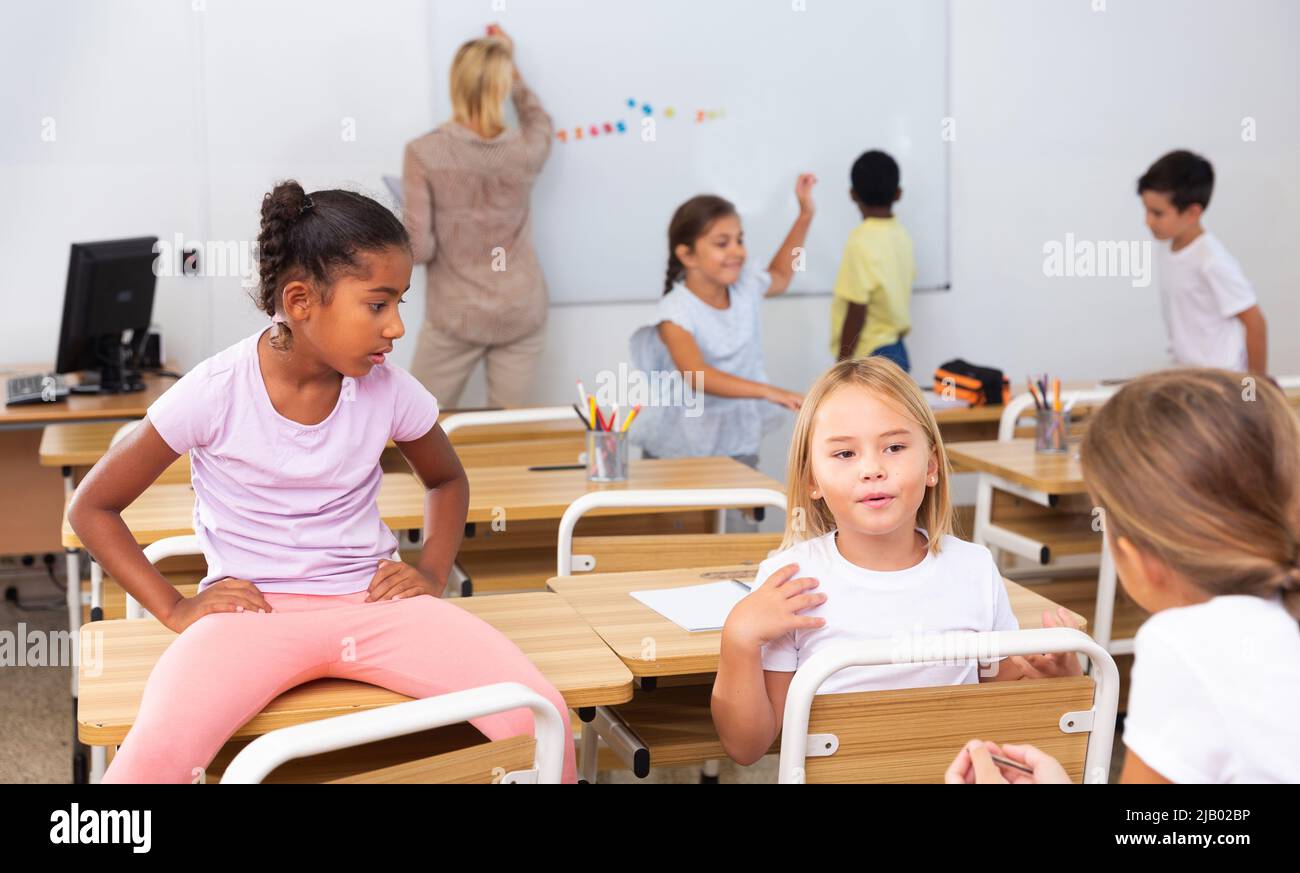 Positive primary school students are talking about homework at desk ...