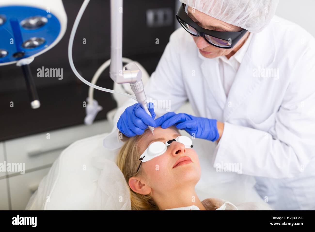 Professional beautician making laser resurfacing to female client face ...