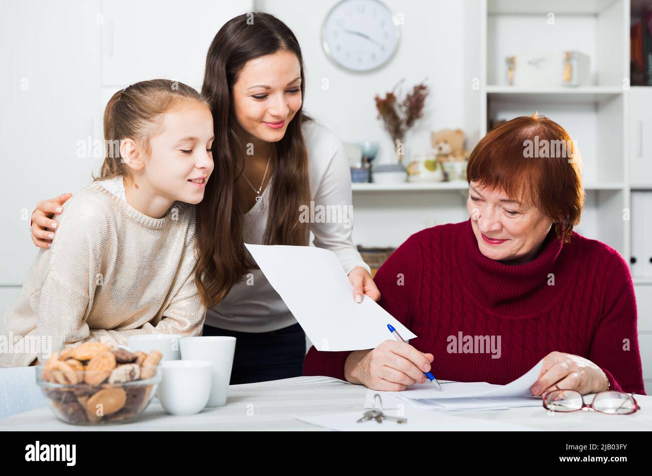 Smiling woman with girl helping elderly mother with paperwork Stock ...
